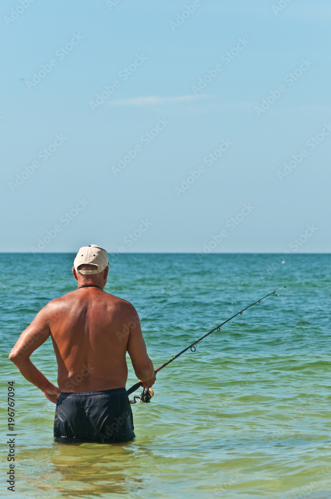Bakc view of a Senior, male wading, relaxing and surf fishing in ...