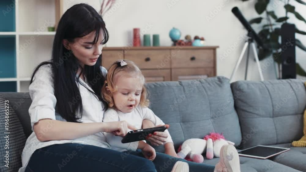 Happy mom and daughter sit on sofa use phone hug woman baby hand love ...