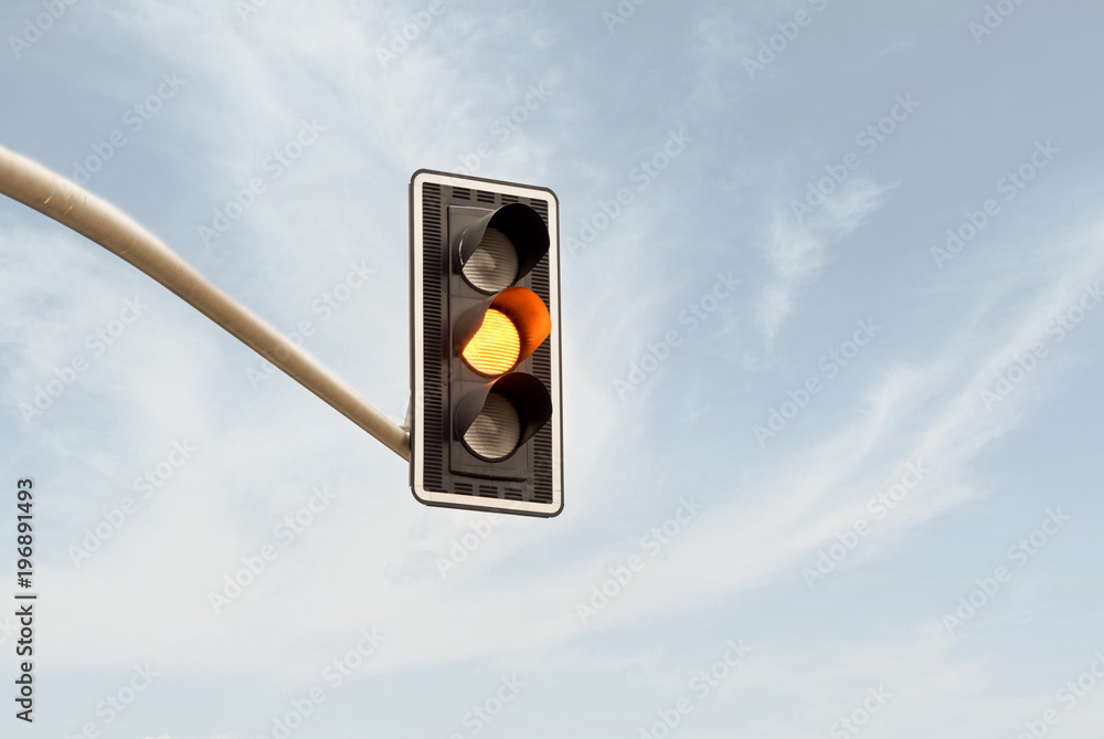 Yellow traffic light on a horizontal white metal beam, isolated on sky ...