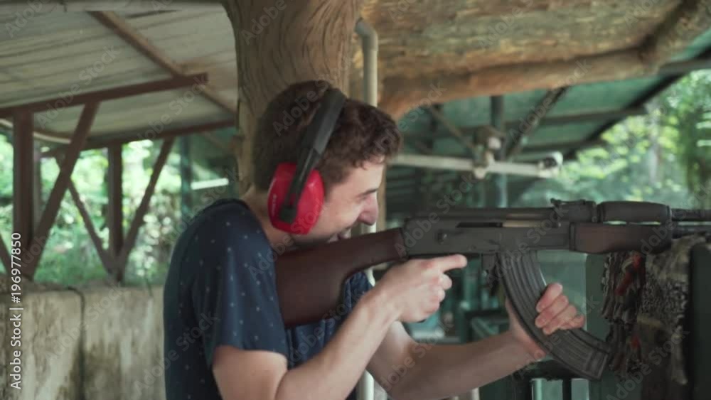 Slow motion: white millennial man smiling while firing ak 47 automatic ...