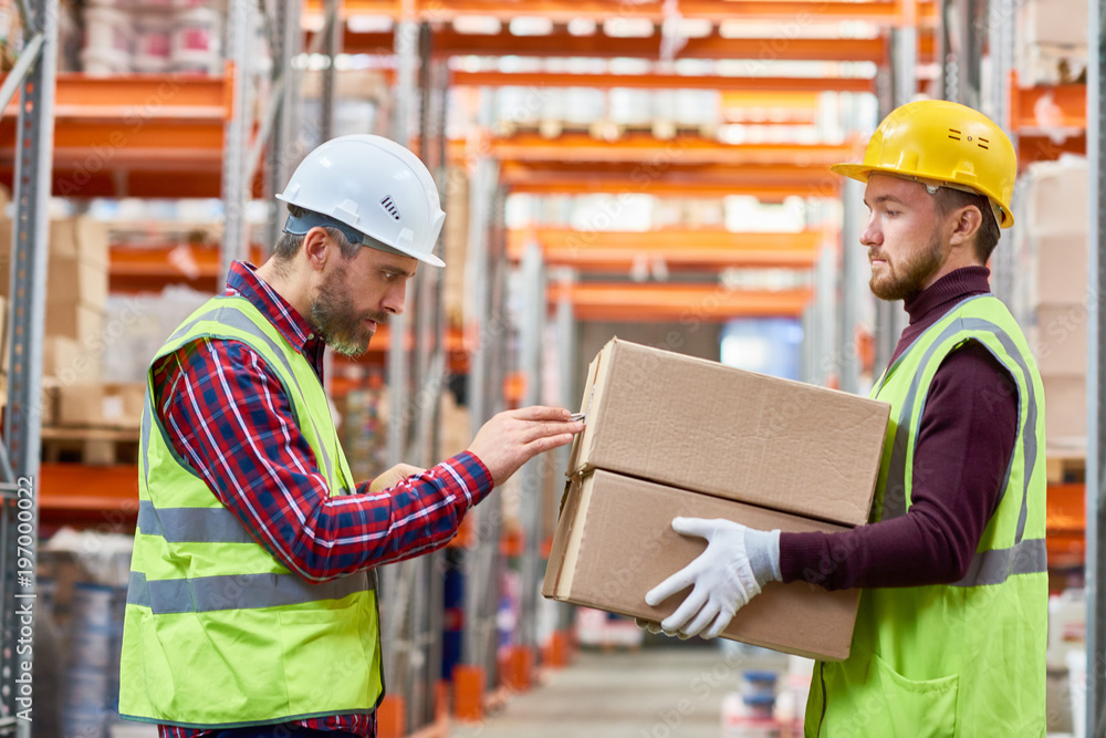 Side view portrait of two shipping workers marking cardboard box for ...