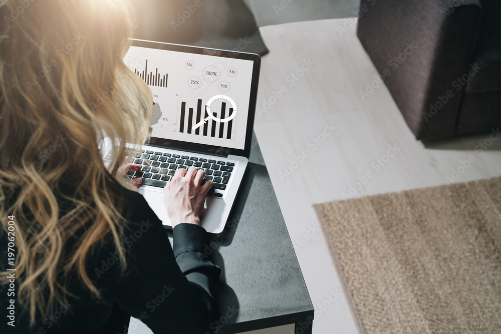 Rear view. Young businesswoman is sitting at table, working on laptop ...