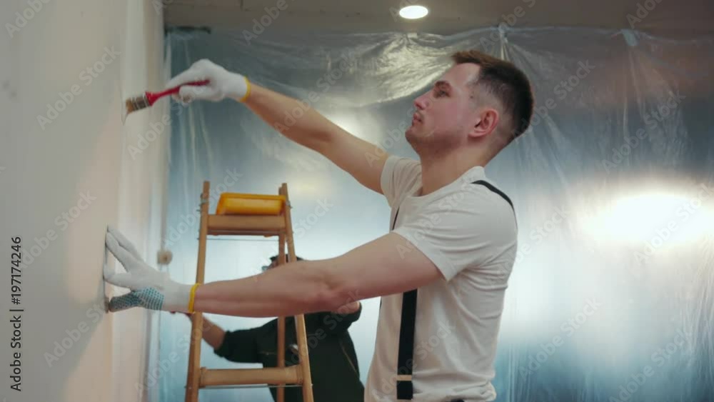 Workmen in the uniforms painting the walls with paint roller and brush ...