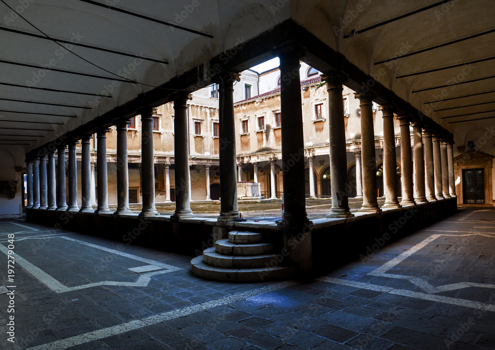 colonnade delimits an ancient cobblestone square, with a well in the ...