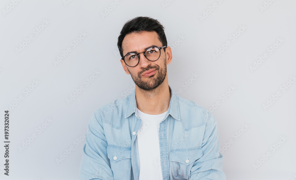 Unshaven handsome Cacuasian male curves lips, looks doubtfully aside ...