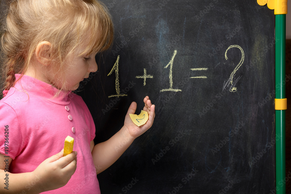 Funny little girl trying solve a simple math problem at the blackboard ...