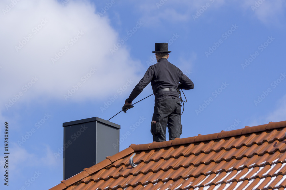 Chimney sweep cleaning a chimney standing on the house roof, lowering ...