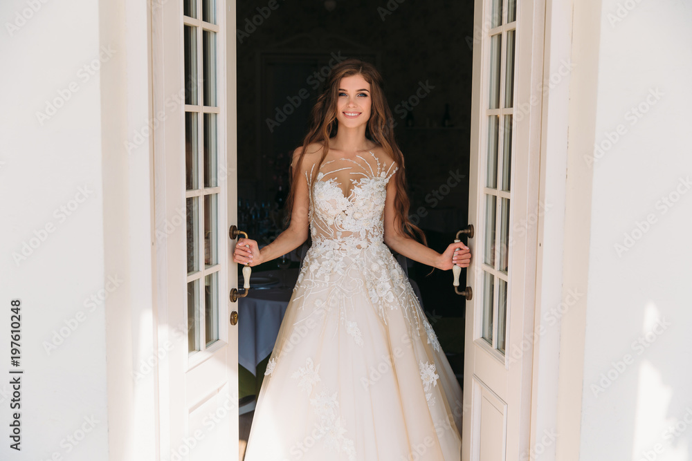 Beautiful bride with attractive long hairs stands near white doors ...