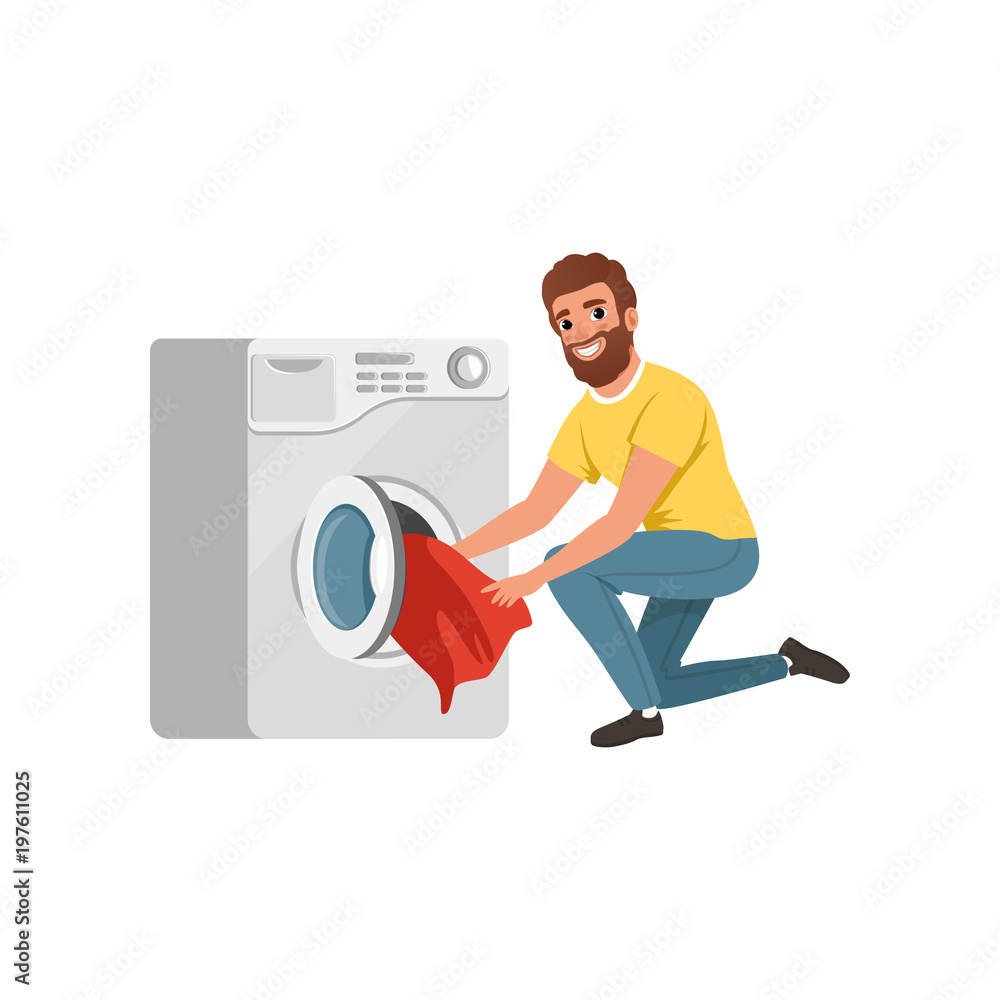 Cheerful bearded man putting dirty clothes into washing machine ...