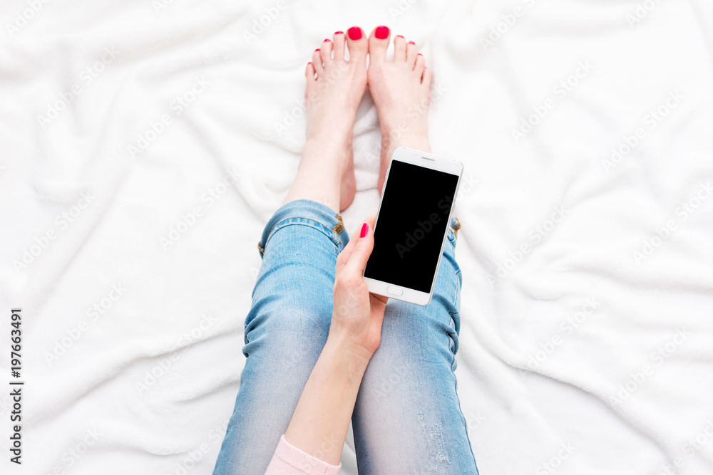 female feet, a girl uses a smart phone, blue jeans, red pedicure ...