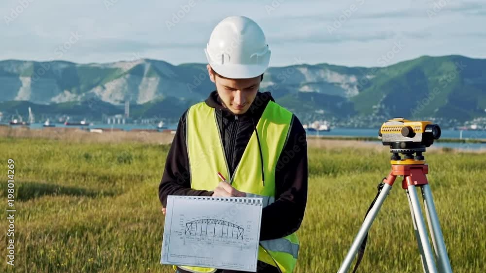 surveyor man in green work clothes and helmet adjusts the equipment ...