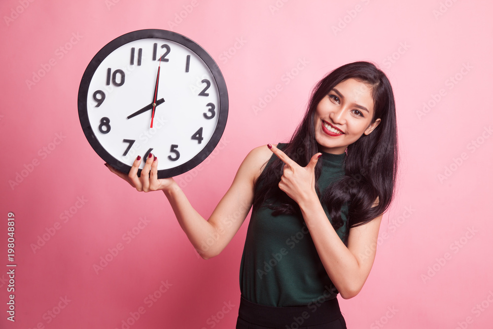 Young Asian woman point to a clock. Stock Photo | Adobe Stock
