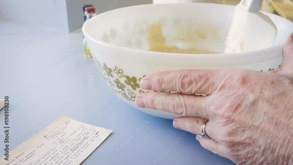Older woman baker stirs batter in a vintage mixing bowl in 4k. The ...