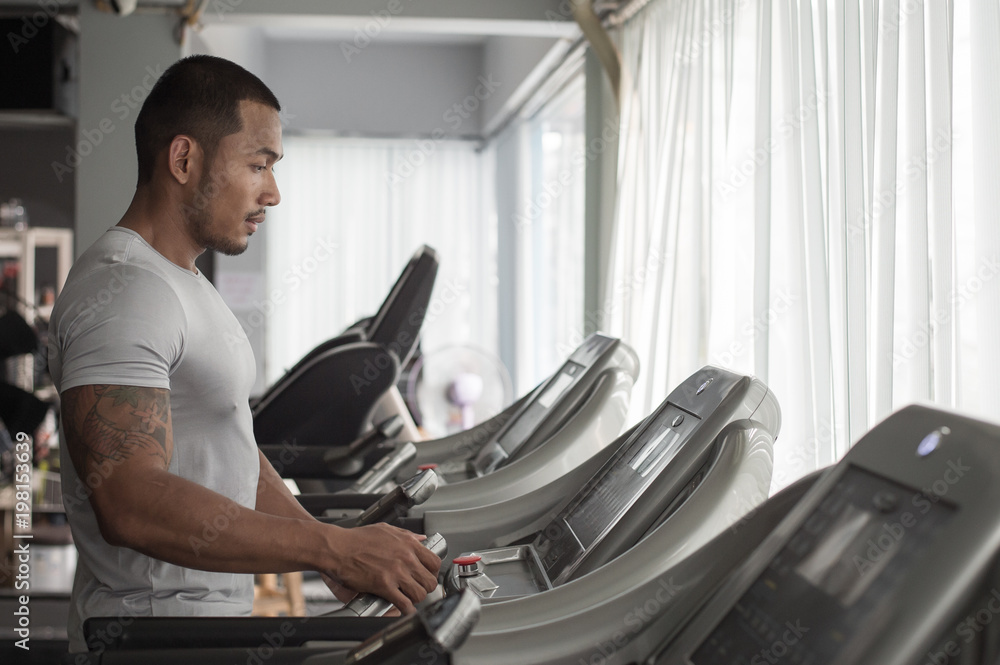 Muscular builder man running in machine treadmill at fitness gym club ...