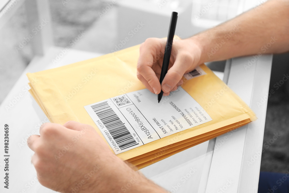 Young man preparing parcel envelopes for shipment to client at home ...