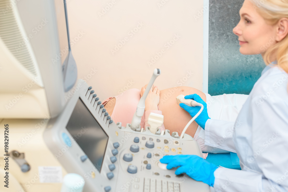 side view of obstetrician gynecologist making ultrasound scanning for ...
