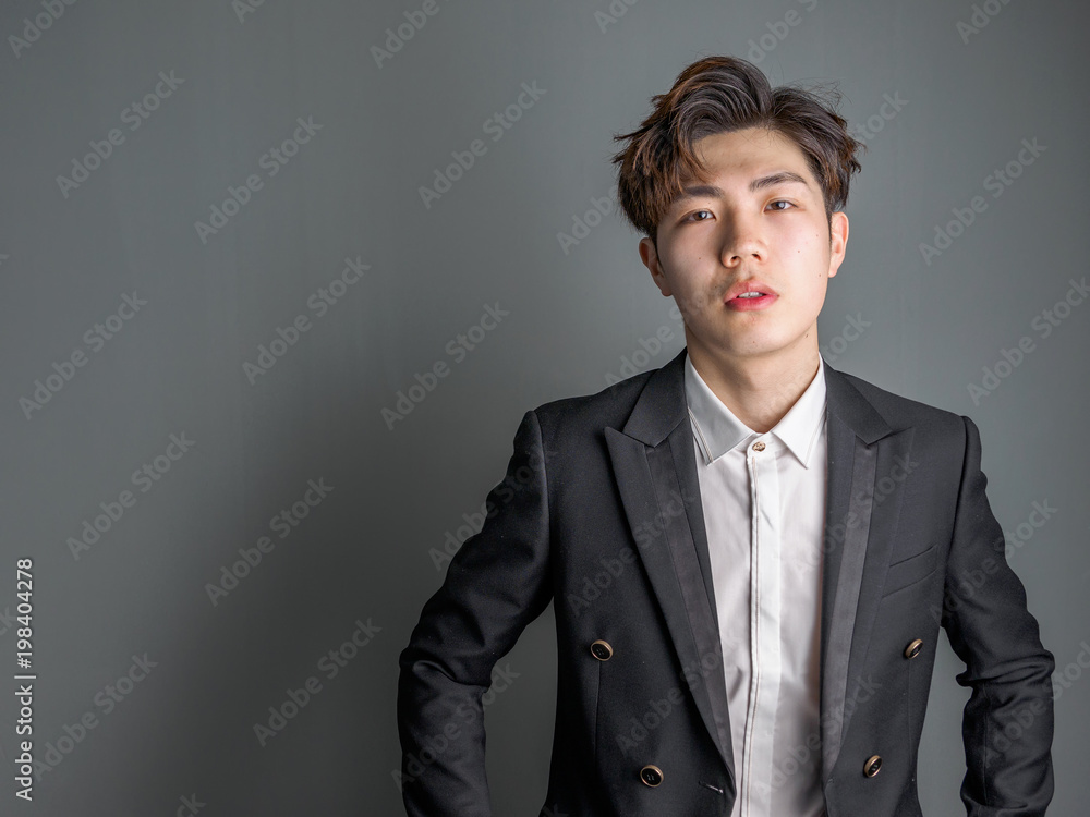 Portrait of a smart young Chinese man standing against gray background ...