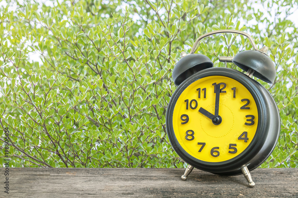Closeup yellow alarm clock show the time in 10 o'clock on wood desk and ...