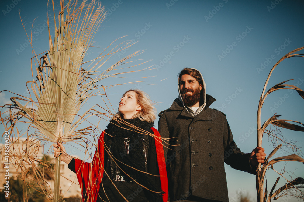 Cool and weird young couple posing outdoors while holding palm tree ...