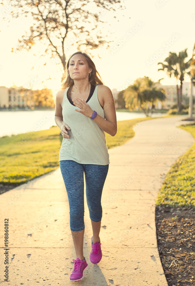 Woman jogging along a pathway in a city park in the early evening. full ...