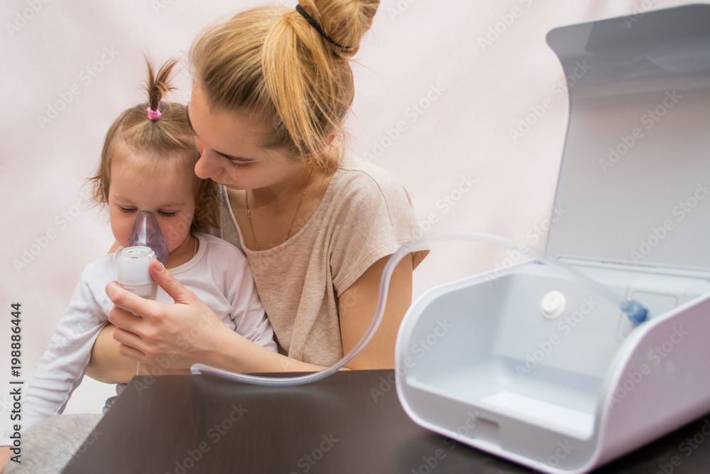 Two year old baby girl inhaling from the inhaler, her mother holding ...