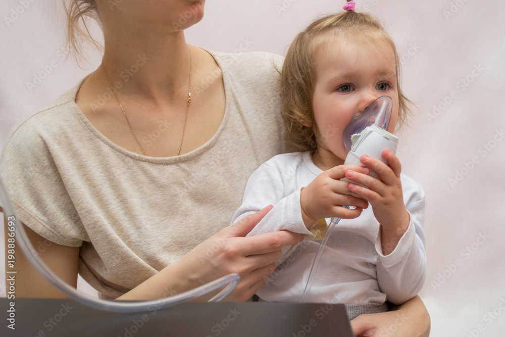 Two year old baby girl inhaling from the inhaler, her mother holding ...