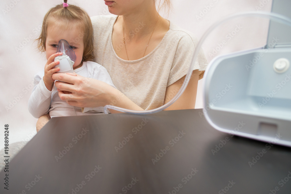 Two year old baby girl inhaling from the inhaler, her mother holding ...