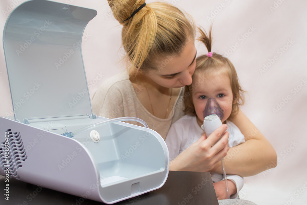 Two year old baby girl inhaling from the inhaler, her mother holding ...