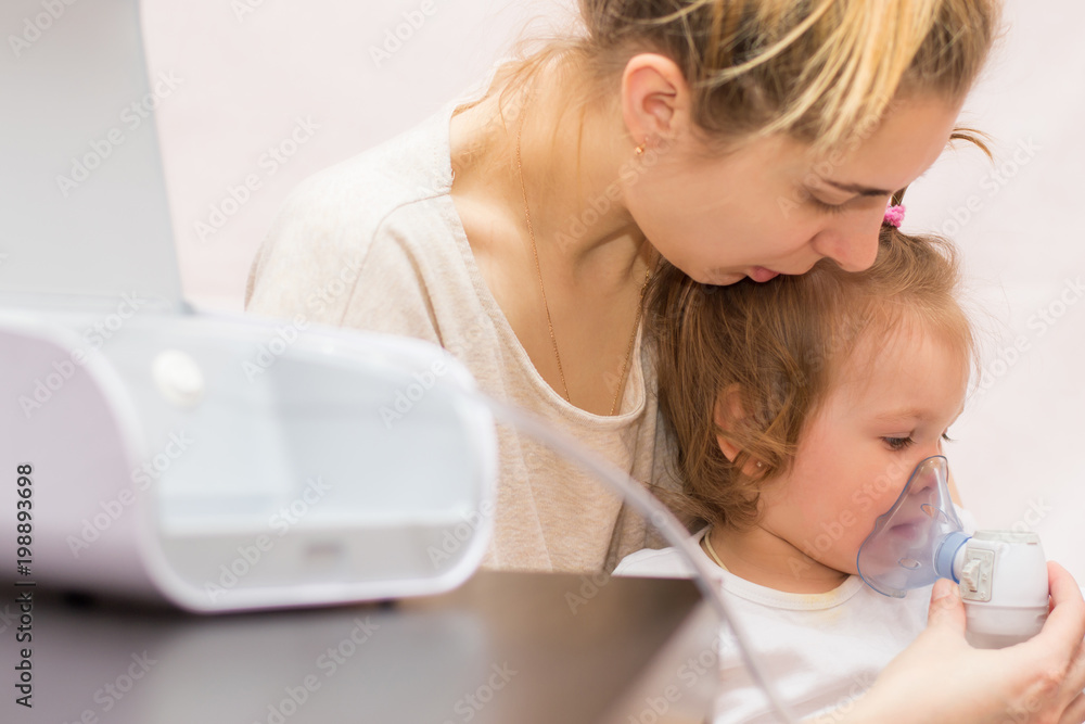 Two year old baby girl inhaling from the inhaler, her mother holding ...