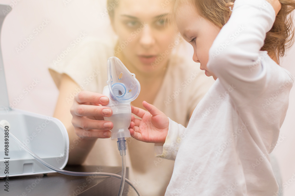 Two year old baby girl inhaling from the inhaler, her mother holding ...