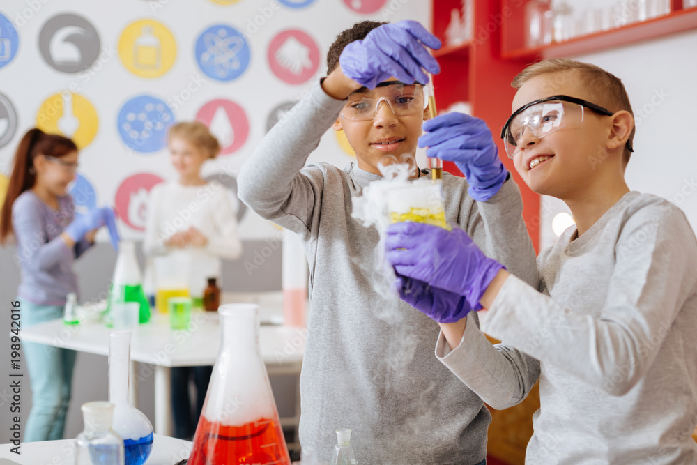 Have a look. Joyful teenage boy showing a flask with fuming liquid in ...