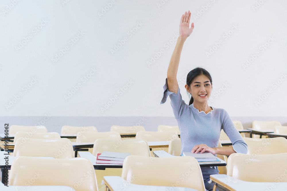 Young woman student raising hands in a classroom showing ready answer ...