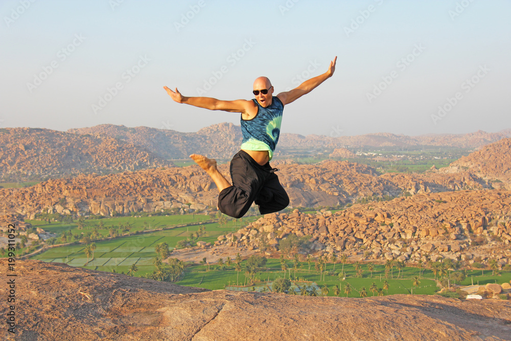 Handsome high jump man. A bald man wearing sunglasses in Hampi, jumps ...