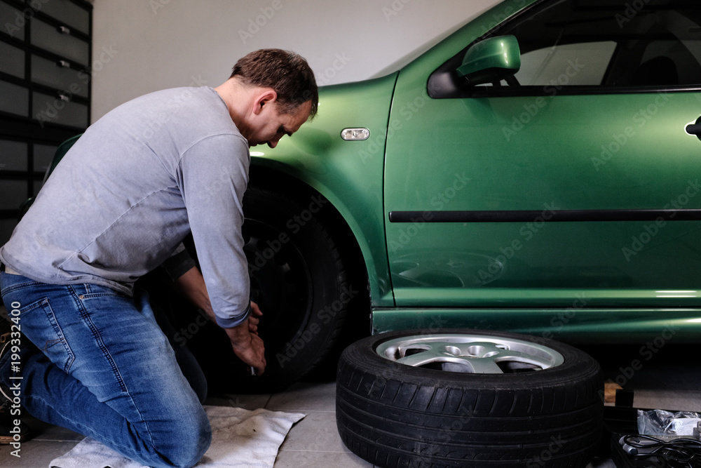 mann beim rad wechseln in der garage Photos | Adobe Stock