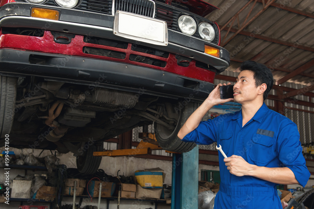 Foto de Asian mechanic speaking on phone under the car to repair the ...