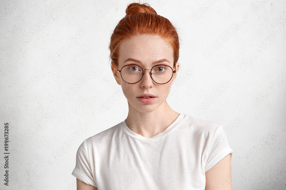 Photo of serious clever redhead female student with ginger hair knot ...