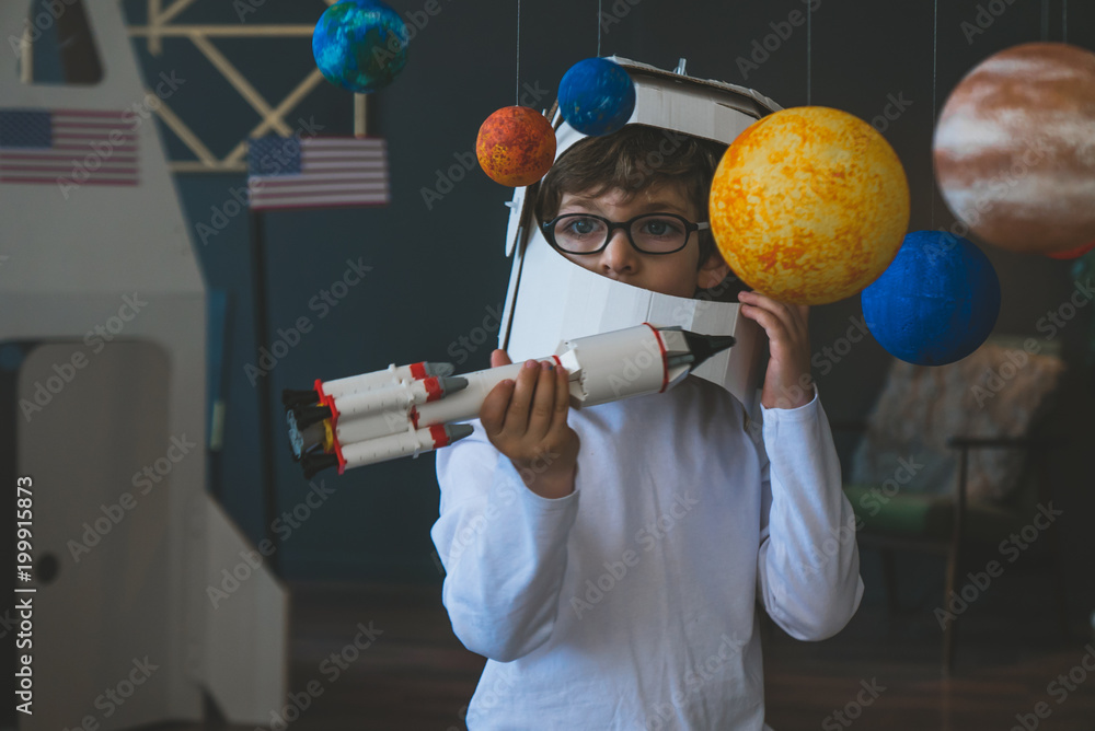 Cute little boy wearing cardboard astronaut helmet flying toy rocket ...
