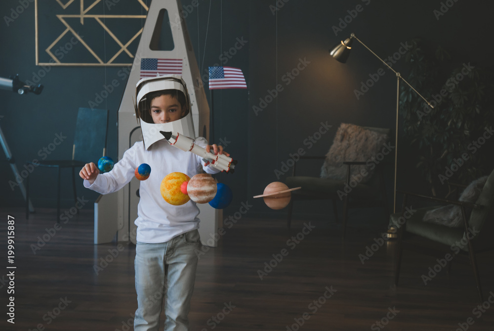 Cute little boy wearing cardboard astronaut helmet flying toy rocket ...