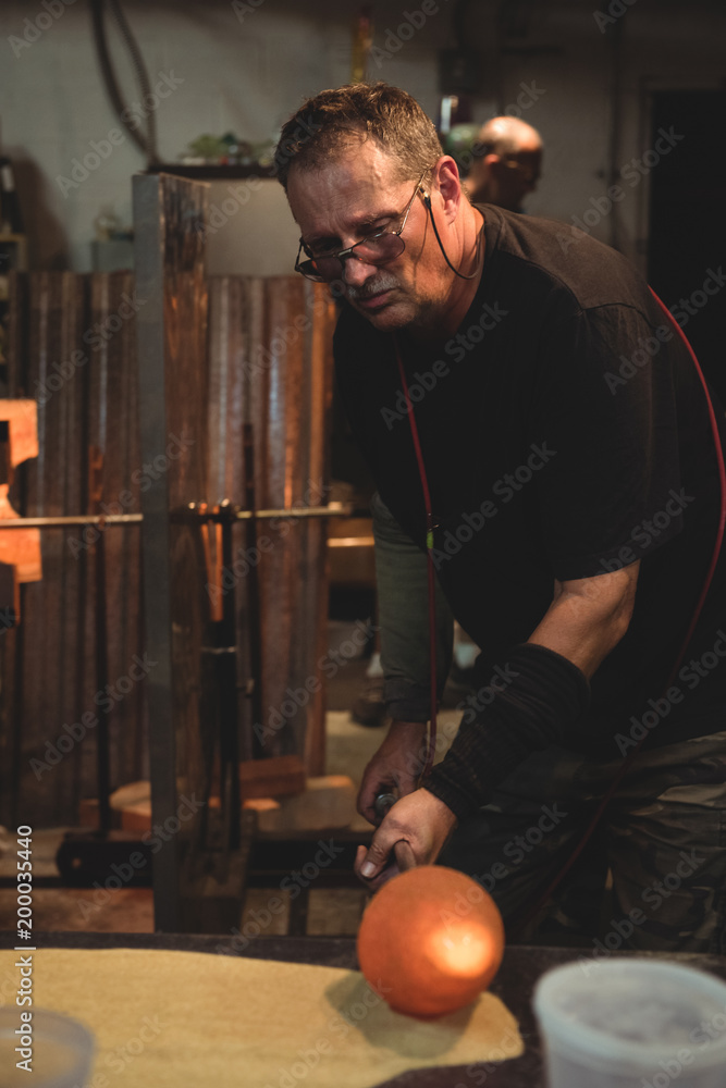 Glassblower rolling molten glass over frit glass on a marver table ...