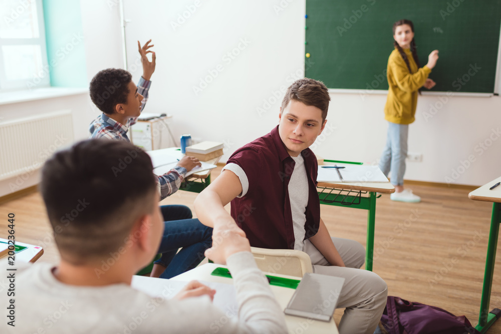 Multicultural high school students doing fist bump and classmates ...