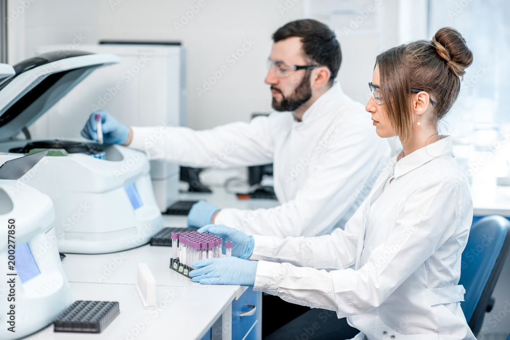 Laboratory assistants making analysis with test tubes and analyzer ...