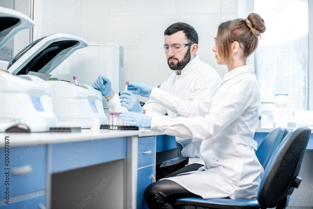 Laboratory assistants making analysis with test tubes and analyzer ...