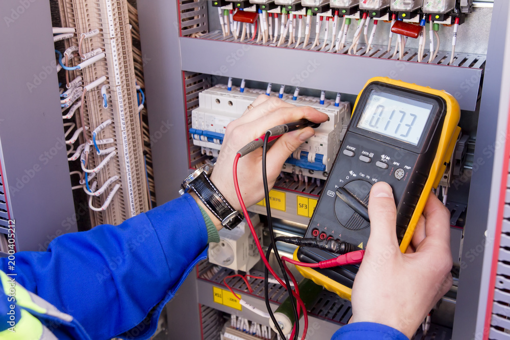 multimeter is in hands of engineer in electrical cabinet. Adjustment of ...