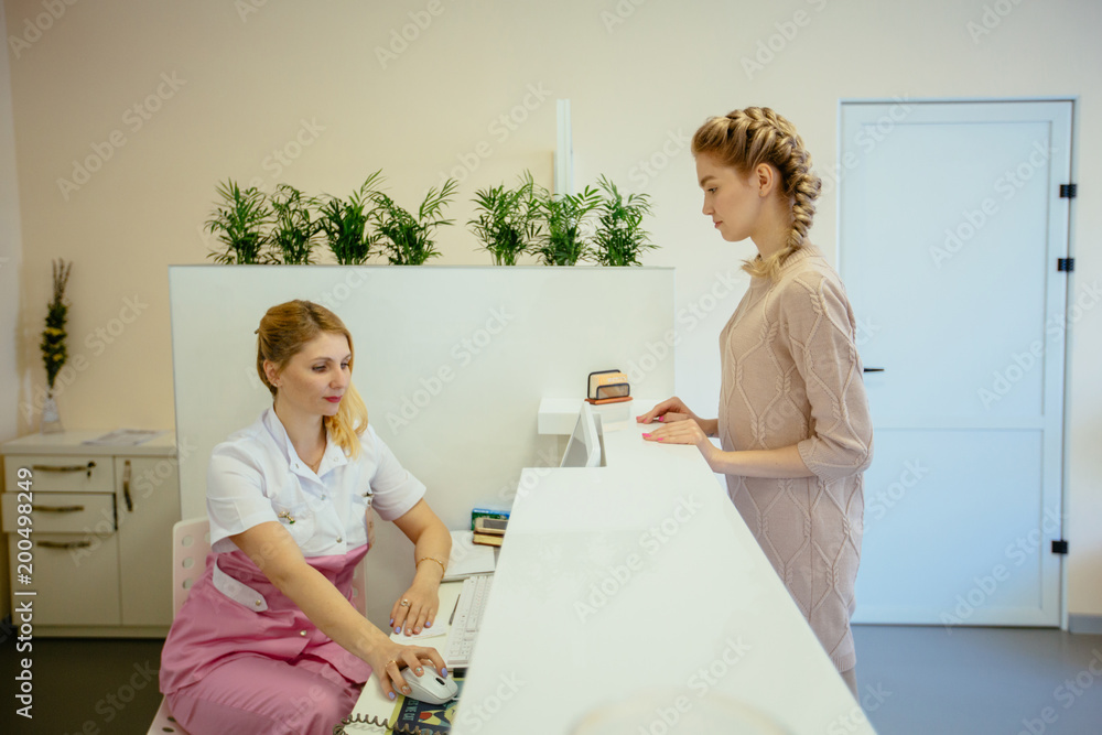 Cute sad blond girl talking with female receptionist in the waiting ...
