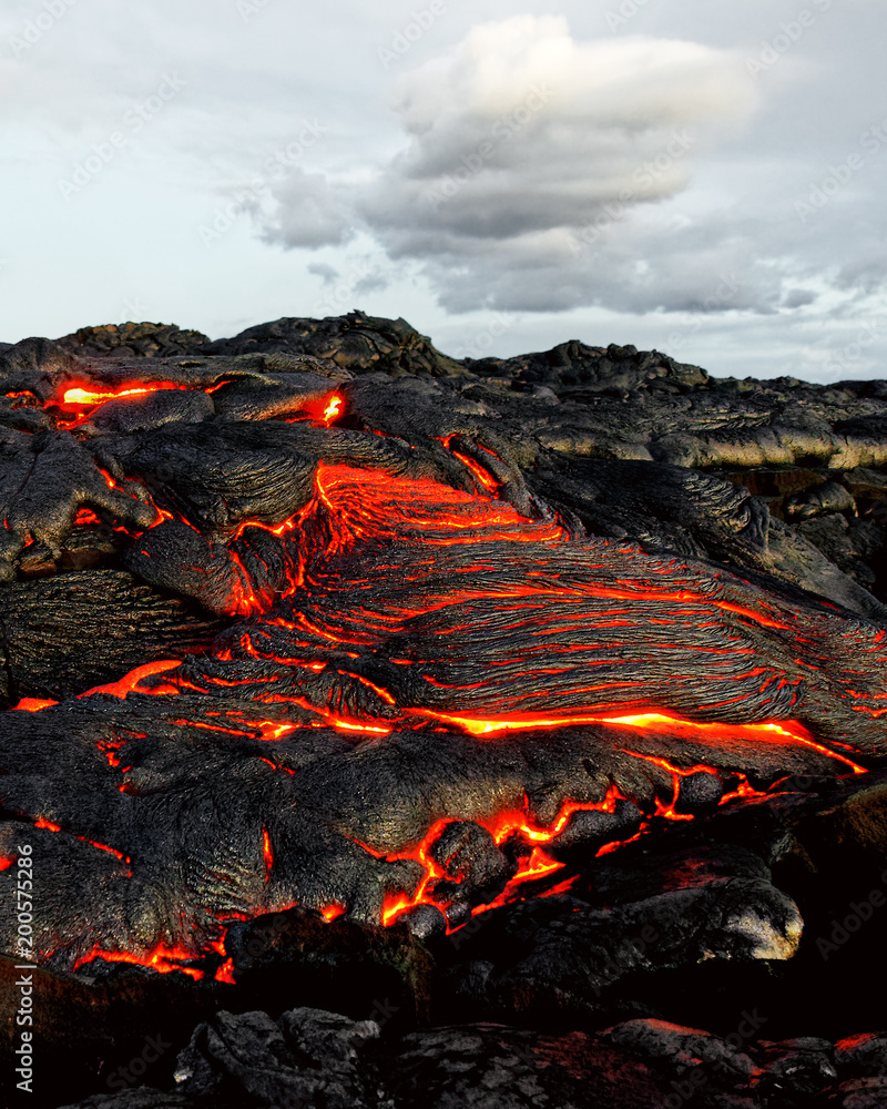 A lava flow emerges from an earth column and flows in a black volcanic ...