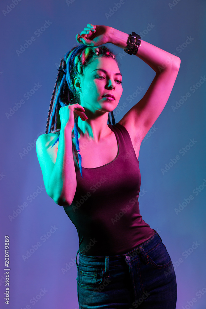 Dancing modern girl with colored dreadlocks. Isolated on a blue ...