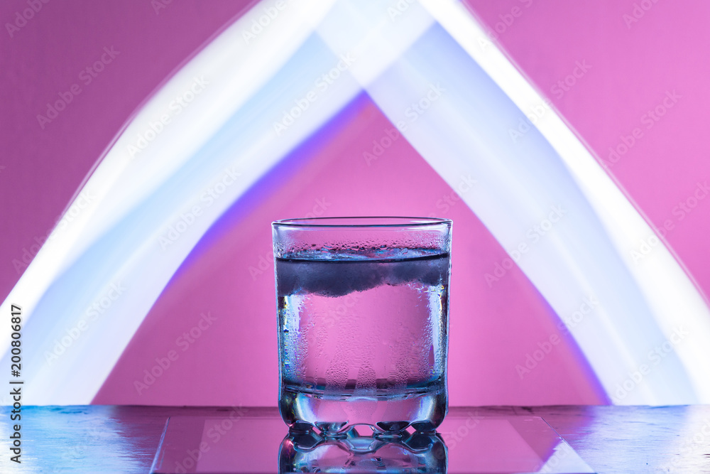 Liquid with ice in a glass on a reflective surface on a reddish ...