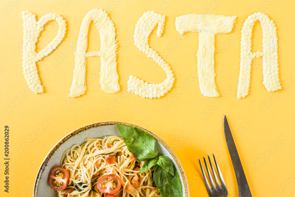 The word pasta is laid out of small pasta next to a plate with head ...