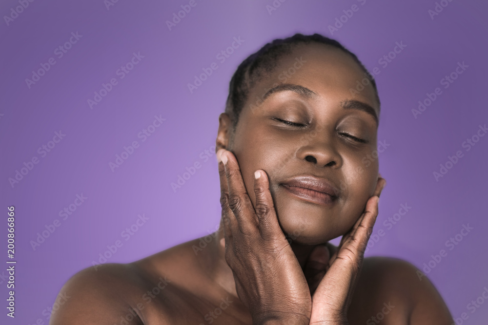 Beautiful African woman touching her cheeks against a purple background ...