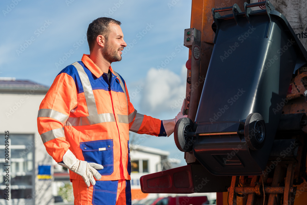 Garbage collection worker putting bin into waste truck for removal ...